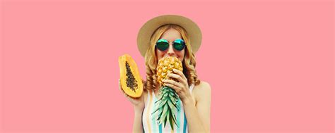 파인애플과 파파야 신선한 열대 육즙이 많은 과일 밀짚 모자 분홍색 배경에 선글라스를 착용하고 있는 행복한 미소 짓는 젊은 여성의