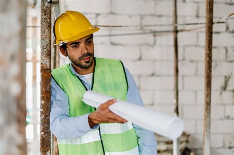 머리에 안전 헬멧을 착용하고 조끼를 입은 건설 현장에서 청사진을 들고 있는 건설 노동자 가리키기에 대한 스톡 사진 및 기타 이미지 가리키기 건설 현장 건설업자