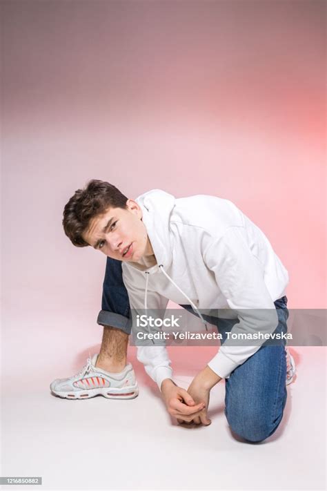 흰색 스웨트 셔츠 청바지와 흰색 운동화를 입고 유행 잘 생긴 젊은 유럽 남성 모델은 상업 사진 촬영을위한 분홍색 배경에 스튜디오에서 포즈를 취하고 카메라를보고 대학교에 대한