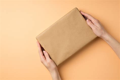 카피 스페이스와 고립 된 베이지 색 배경에 크래프트 종이 선물 상자를주는 소녀의 손의 1 인칭 최고 보기 사진 갈색에 대한 스톡