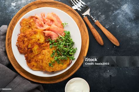감자 팬케이크 오래된 검은 테이블 배경에 소박한 접시에 크림 파 마이크로 그린 붉은 연어와 소스와 함께 집에서 만든 감자 팬