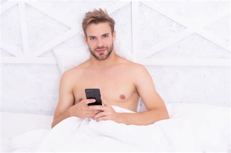Premium Photo Smiling Man Reading Message On Phone In White Bedroom