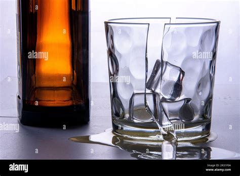 Empty Rum Bottle And Broken Glass In Two Halves With Three Ice Cubes