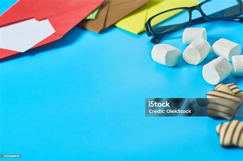 흩어진 과자 줄무늬 사탕 안경 근처의 원통형 마시멜로 흰색 빈 종이 시트가 있는 봉투가 파란색 책상 위에 놓여 있습니다 사랑