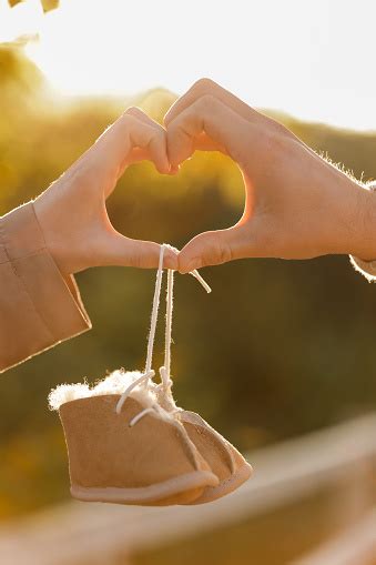 남자와 임신한 아내는 손으로 하트 제스처를 하고 자연의 가을 배경에서 따뜻한 아기 신발을 들고 있다 아기를 기다리는 미래의 부모 어머니의 날과 여성의 날의 개념 2명에 대한