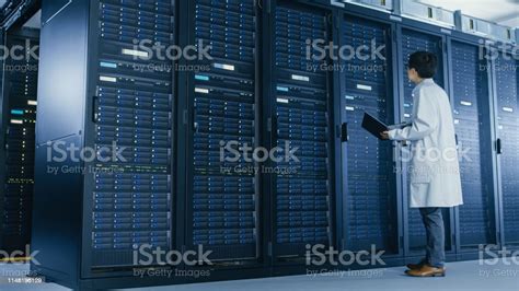 데이터 센터 서버 랙 옆에 흰색 코트를 착용 한 남성 It 전문가는 랩톱 컴퓨터를 사용 하 여 유지 관리 진단 도구를 실행 하 고 데이터베이스가 최적의 수준에서 작동 하도록