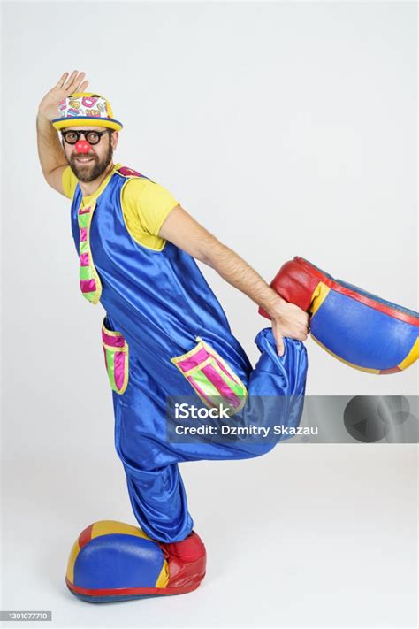 광대는 밝은 파란색과 노란색 정장 안경과 모자를 쓰고 감정적으로 노는 남자입니다 어릿광대 서커스 공연자에 대한 스톡 사진 및