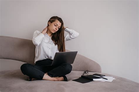 긴 머리를 가진 피곤한 갈색 머리 사업가는 열심히 일한 후 옆으로 뻗어있는 노트북을 사용하여 소파 다리에 앉아 있습니다 꽤 과부하 된 히스패닉 소녀는 피로를 느낍니다 외로움