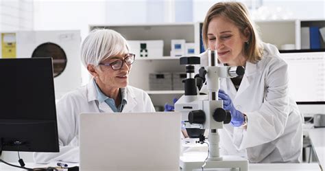 실험실 파트너 연구 및 과학자와 함께 의료실에서 임상 테스트를위한 현미경을 가진 여성 깨끗한 시설에서 줌 렌즈 기술을 사용한