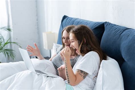 Two Smiling Excited Lesbians Using Laptop In Bed In Morning Stock
