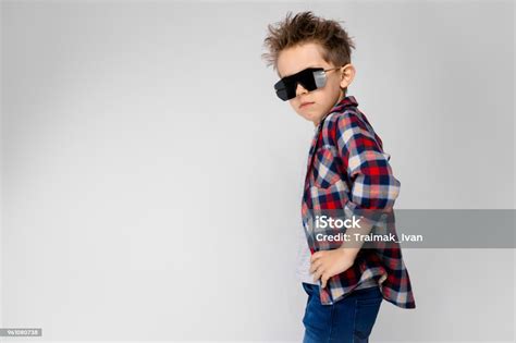 잘생긴 소년 격자 무늬 셔츠 회색 셔츠와 청바지에 회색 배경에 서 있다 검은 선글라스에 소년입니다 하프 깨어 는입니다 소년은 그의 엉덩이에 그의 손을 넣어 감정에 대한 스톡