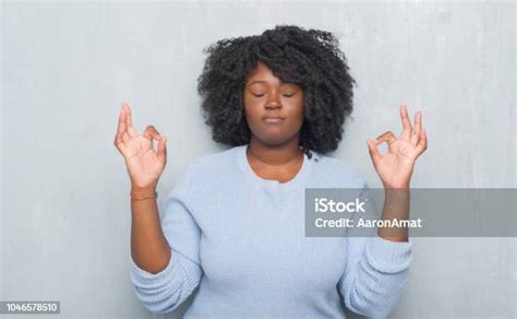 젊은 아프리카계 미국인 여자 겨울 스웨터를 입고 회색 그런 지 벽에 휴식과 명상 손가락으로 제스처를 하 고 폐쇄 눈으로 웃 고 요가 개념 가을에 대한 스톡 사진 및 기타