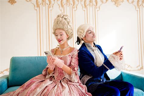 바로크 양식의 의상을 입은 우아한 커플이 호화로운 역사적인 환경에서 스마트 폰을 사용하고 있습니다 16 17 살에 대한 스톡