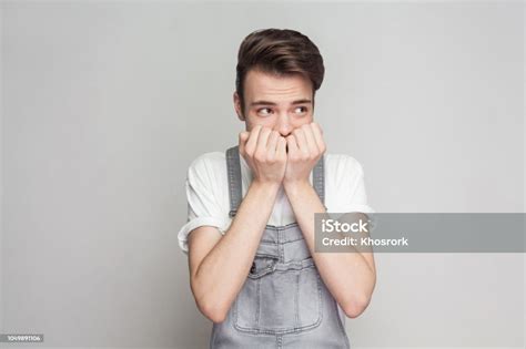 긴장 젊은 갈색 머리 남자의 서 하 고 찾고 흰색 T셔츠와 데님 바지와 캐주얼 스타일에서 걱정 얼굴로 손톱을 물어 뜯고 초상화 남자에 대한 스톡 사진 및 기타 이미지