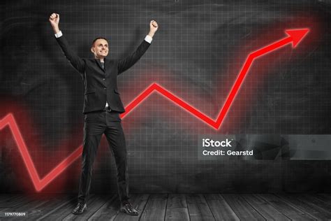 검은 색 그래프 가루 벽 근처 그의 뒤에 올라가는 빨간색 그래프 화살표와 승리 제스처에 팔을 올리는 행복 한 사업가의 전면 전체 길이보기 개발에 대한 스톡 사진 및 기타