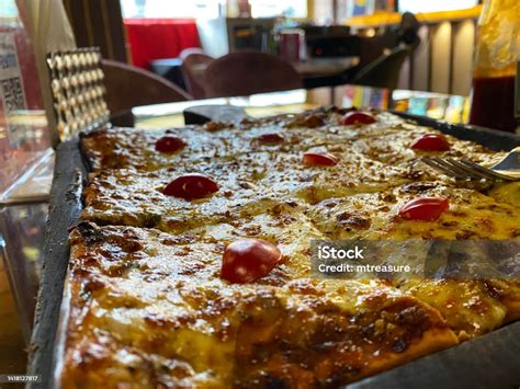 얇게 썬 갓 구운 사각형 Margherita 피자 녹인 버팔로 모짜렐라 치즈 풍부한 토마토 마리나라 소스와 체리 토마토 반쪽 토핑 금속 포크 전경에 초점을 맞춘 레스토랑