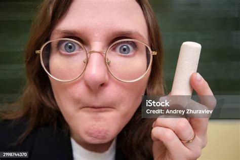 교사는 놀라움과 흥분의 표정으로 칠판 앞에 서서 손으로 분필 조각을 들고 교실에서 학생의 예상치 못한 훌륭한 대답에 반응합니다