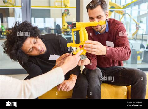 Two Engineers Closely Inspecting A Robotic Arm Model During A Technical