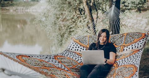 화창한 여름 공원의 해먹에 누워 노트북으로 작업하는 소녀 프리랜서 여성 힙스터는 노트북을 들고 편안하고 웃고 있다 프리랜서 개념입니다 학생 연구 여름 방학 사진