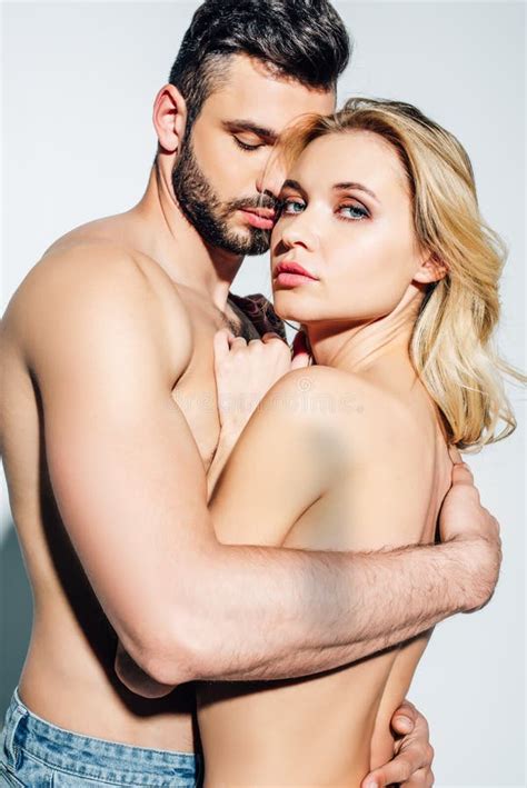 Shirtless Man Hugging Naked Blonde Woman Looking At Camera On White