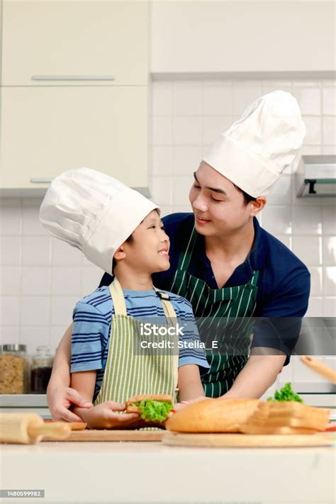 앞치마 요리사 모자를 쓴 행복한 미소를 짓는 아시아 아버지와 아들 아이가 부엌에서 함께 식사를 요리하고 아빠 부모는 간단한 식사를 준비하는 소년 아이를 돕고 귀여운 가족