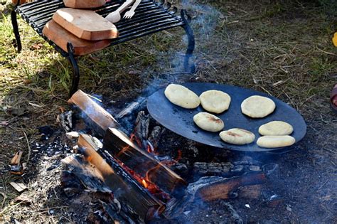 통나무 널빤지 판자로 구성된 장작에 놓인 철 팬을 사용하여 구운 만두 또는 쇼트브레드 쿠키를 클로즈업한 사진 폴란드의 철제 창살과 무성한 잔디밭 옆에서 볼 수 있습니다 0