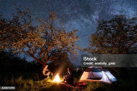 로맨틱 커플 등산객 나무와 아름 다운 밤 하늘 가득 별과은 하 수 아래 텐트 근처 모닥불에 앉아 밤 캠핑 경외감에 대한 스톡 사진 및 기타 이미지 Istock