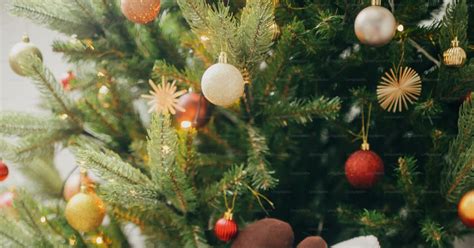 선물과 축제 조명이 있는 현대적인 장식된 크리스마스 트리 아래 산타 모자를 쓴 귀여운 순록 장난감 빨간색과 금색 싸구려 스칸디나비아 방 장식이 있는 크리스마스 트리의 큰