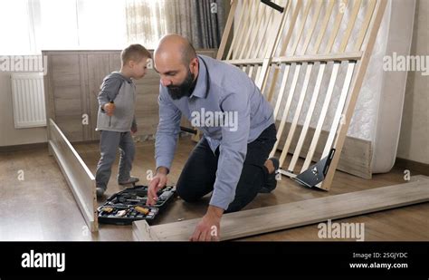 Dad And Son Are On The Floor Assembling Parts For A New Bed In The