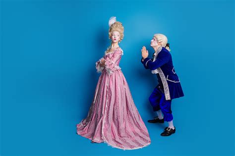 우아한 바로크 양식의 의상을 입은 커플이 생생한 파란색 배경을 배경으로 포즈를 취하며 역사적인 패션의 조화를 보여줍니다 16 17 살에 대한 스톡 사진 및 기타 이미지
