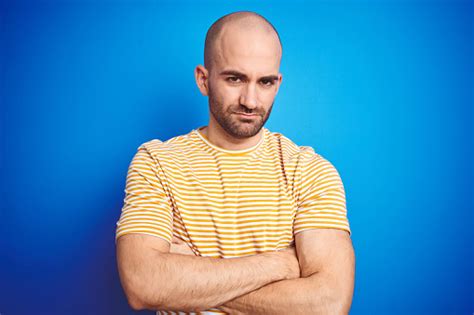 파란색 고립 된 배경 회의적이고 긴장한 위에 캐주얼 한 티셔츠를 입은 수염을 가진 젊은 대머리 남자 교차 된 팔로 얼굴에 표정을 거부 부정적인 사람 T 셔츠에 대한 스톡