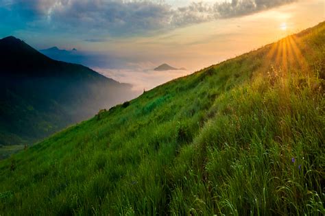 일출 좋은 날씨에 산 풍경입니다 녹색 잔디 가파른 언덕 안개 골짜기와 밝은 푸른 하늘 아래 먼 산 태양 흰 구름을 발생 시켜 조명 자연의 아름다움입니다 0명에 대한 스톡