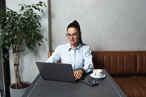 젊은 성공적인 자영업 프리랜서 여성은 카페테리아에서 노트북 컴퓨터로 일하면서 커피를 마시며 자유를 즐기고 있습니다 커피 숍에서 일하는 새로운 중소기업 소유자 사업가 계획에