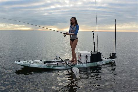 A Woman Standing On Top Of A Kayak While Holding A Fishing Rod And Reel