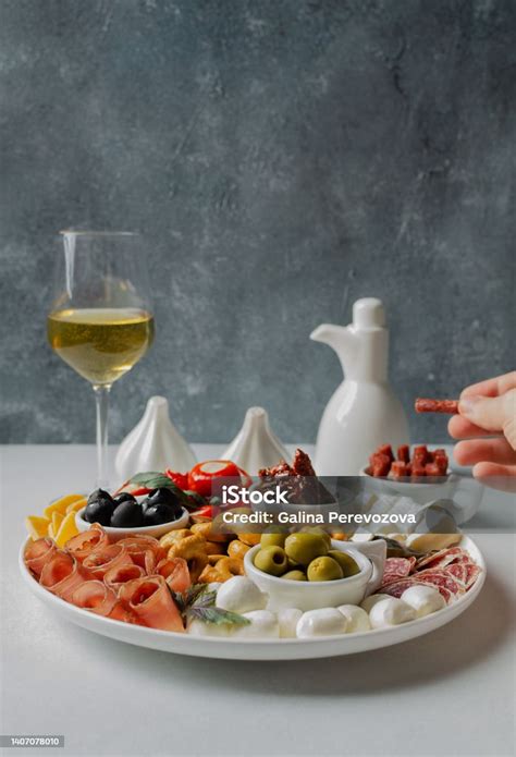 클래식 이탈리아 전채 또는 타파스 화이트 와인 스낵 세트 치즈 품종 검은 색과 녹색 올리브 피클 프로슈토 디 파르마 토마토 살라미 타랄리니 남자 손이 쵸 리조를 복용 그릇에