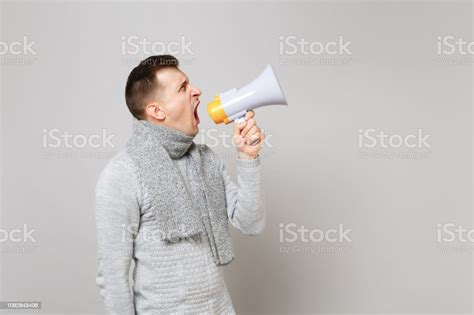 회색 스웨터에 있는 젊은이 측면 비명 스튜디오에 회색 벽 배경에 고립 된 확성기에 스카프 건강 패션 라이프 스타일 사람들이 진심으 감정 추운 계절 개념 복사 공간을 비웃는