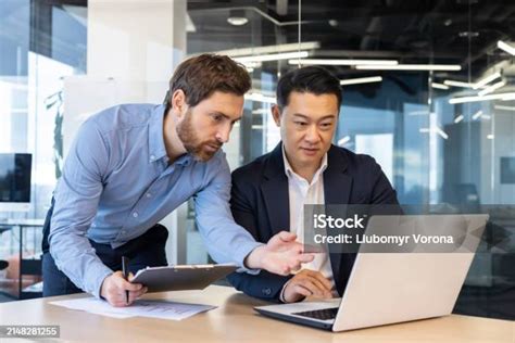 비즈니스 미팅 두 명의 사업가가 전략과 계획에 대해 진지하게 논의하고 직장에서 사무실 내부 문서가 있는 테이블에 앉아 노트북 화면을 보면서 의사 소통에 대해 논의합니다