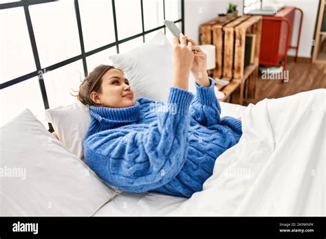 Young Beautiful Hispanic Woman Make Selfie By Smartphone Lying On Bed