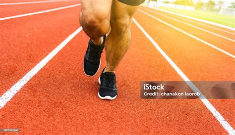 다리를 닫으십시오 스포츠 경기장에서 트랙에서 달리는 운동복을 입은 젊은 중국 남자 실외에서 조깅하는 남자 조깅이 결승선을 통과합니다 아침에 운동하십시오 건강하고 활동적인