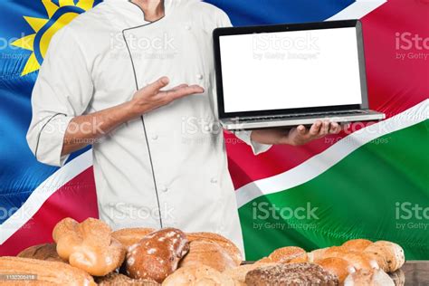 나미비아 플래그와 빵 배경에 노트북을 들고 나미비아 베이커 요리사가 복사 공간에 대 한 균일 한 포인팅 빈 화면을 착용 고급 요리에 대한 스톡 사진 및 기타 이미지 Istock