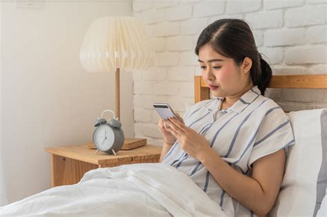 젊은 아시아 여자 거짓말 에 침대 사용 스마트폰 용 채팅 에 아침 25 29세에 대한 스톡 사진 및 기타 이미지 25 29세 Brand Name Online