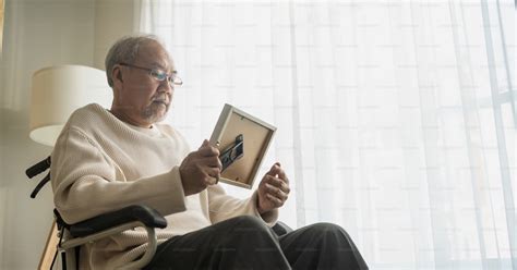 아시아 노인 남성은 휠체어에 혼자 앉아 가족 사진을 본다 연로한 장성한 할아버지는 은퇴 후 요양원에 머무는 동안 친척과 아내를 그리워하며 외롭고 슬퍼합니다 사진