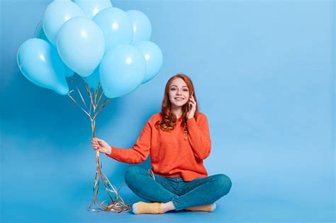 캐주얼 한 스웨터와 청바지에 행복한 젊은 빨간 머리 여자 소녀 푸른 배경에 고립 포즈 생일을 축하하는 여자 헬륨 풍선을 들고