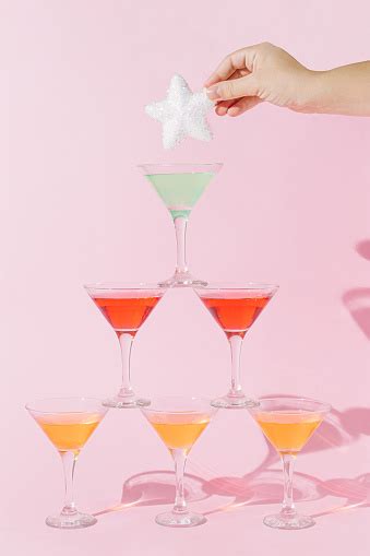 분홍색 배경에 별과 여자의 손이 있는 크리스마스 트리 모양으로 배열된 화려한 칵테일 잔 새해 파티 또는 축하 최소한의 개념