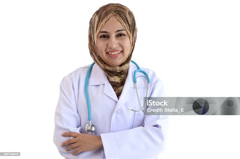 하얀 배경에 팔짱을 끼고 서 있는 실험복을 입고 전통적인 히잡 스카프를 두른 의사 청진기를 들고 웃고 있는 아름다운 중년의 아시아 무슬림 여성 의사의 초상화 35 39세에