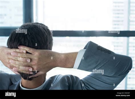 Businessman Looking Through Window With Hands Behind Head Rear View