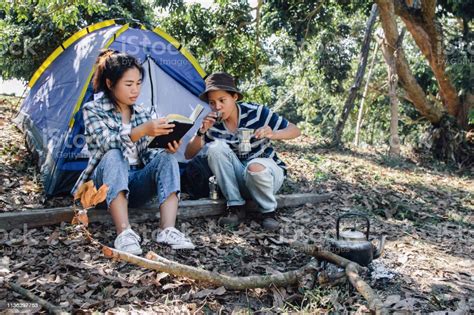 앉아있는 젊은이와 여성은 텐트 밖에 서 책을 읽고 차를 마시는 것입니다 숲에서 우정 캠핑 가죽에 대한 스톡 사진 및 기타 이미지 Istock