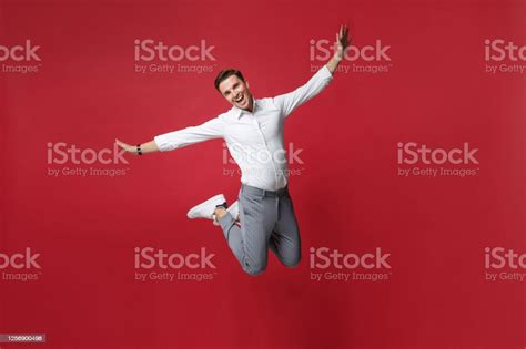 흰색 셔츠를 입은 재미있는 젊은 사업가 밝은 빨간색 배경 스튜디오 초상화에 고립 된 포즈를 취하는 회색 바지 성취 경력 재산 사업 개념 복사 공간을 모의합니다 점프 손을