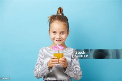 웃는 아이 소녀는 오렌지 주스를 마시고 좋은 분위기를 가지고 있으며 파란색 고립 된 배경에 서 있습니다 4 5세에 대한 스톡