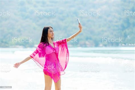 해변에서 걷고 여름 화창한 날에 셀카를 찍는 스마트 폰을 사용하는 행복한 젊은 아름다운 아시아 여성 꽤 섹시한 소녀는 야외 라이프 스타일과 여름 휴가와 함께 즐기고 재미를